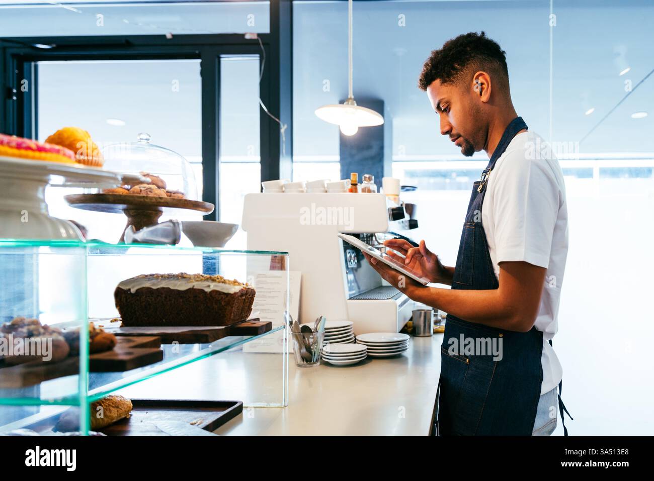 Side view of Black male baker with apron using tablet standing at ...