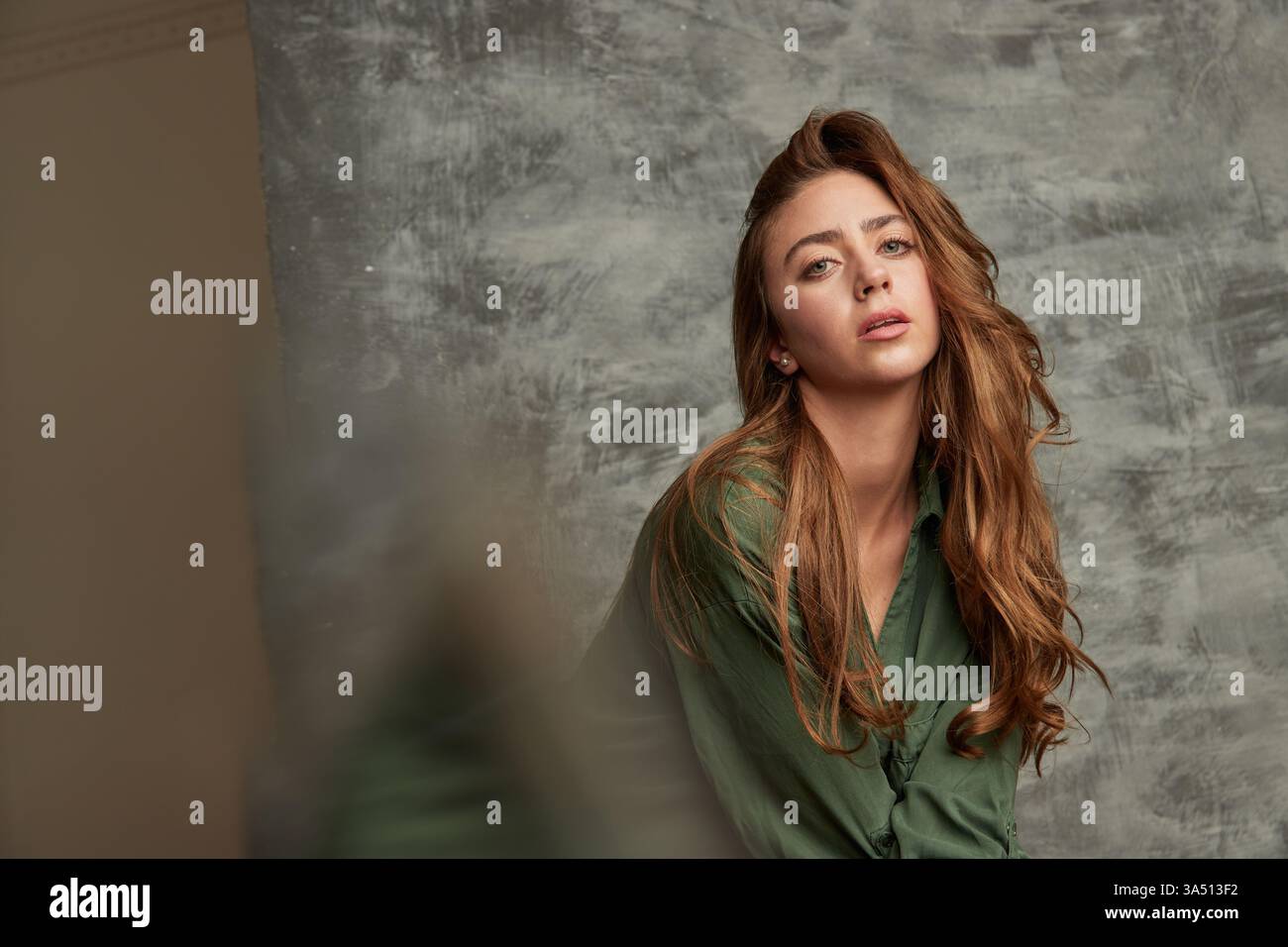 Serious Hispanic female leaning forward with arms crossed against gray ...