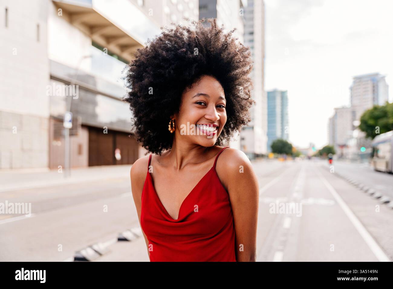 Smiling Black woman with afro standing with hands behind back on city ...