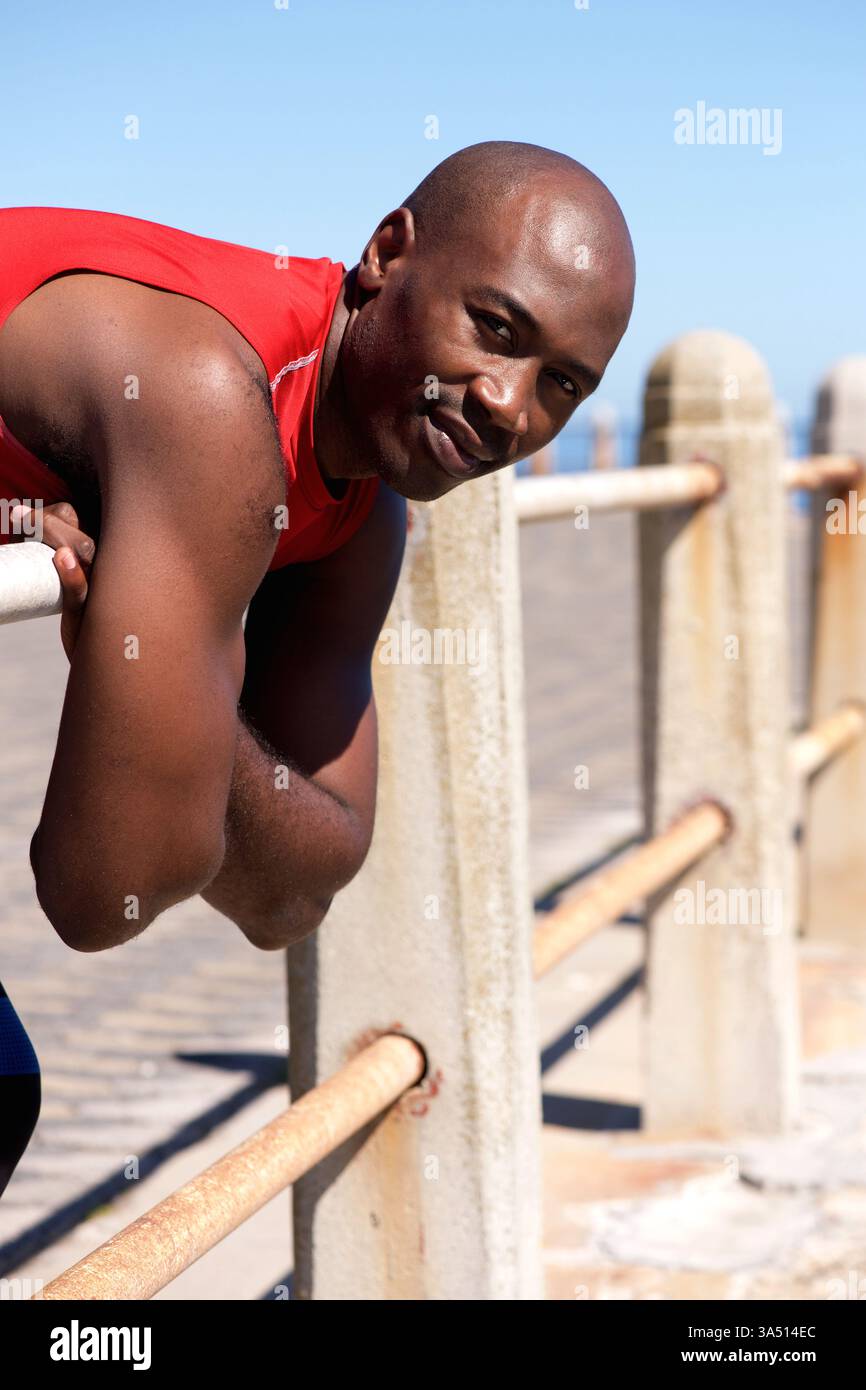 Serious Black man leaning forward on metal railing outdoors on sunny ...