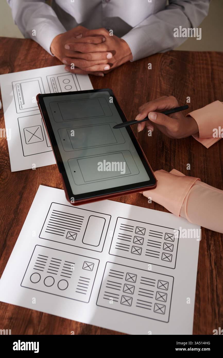 Hands of UI designer pointing at tablet computer with mockup when ...