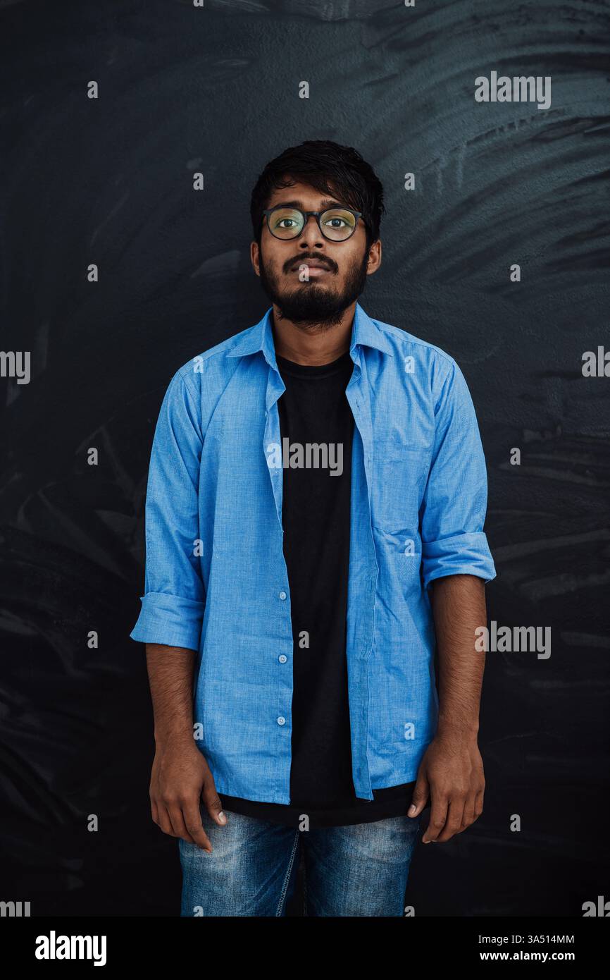 Serious Indian man with beard wearing eyeglasses standing against dark ...