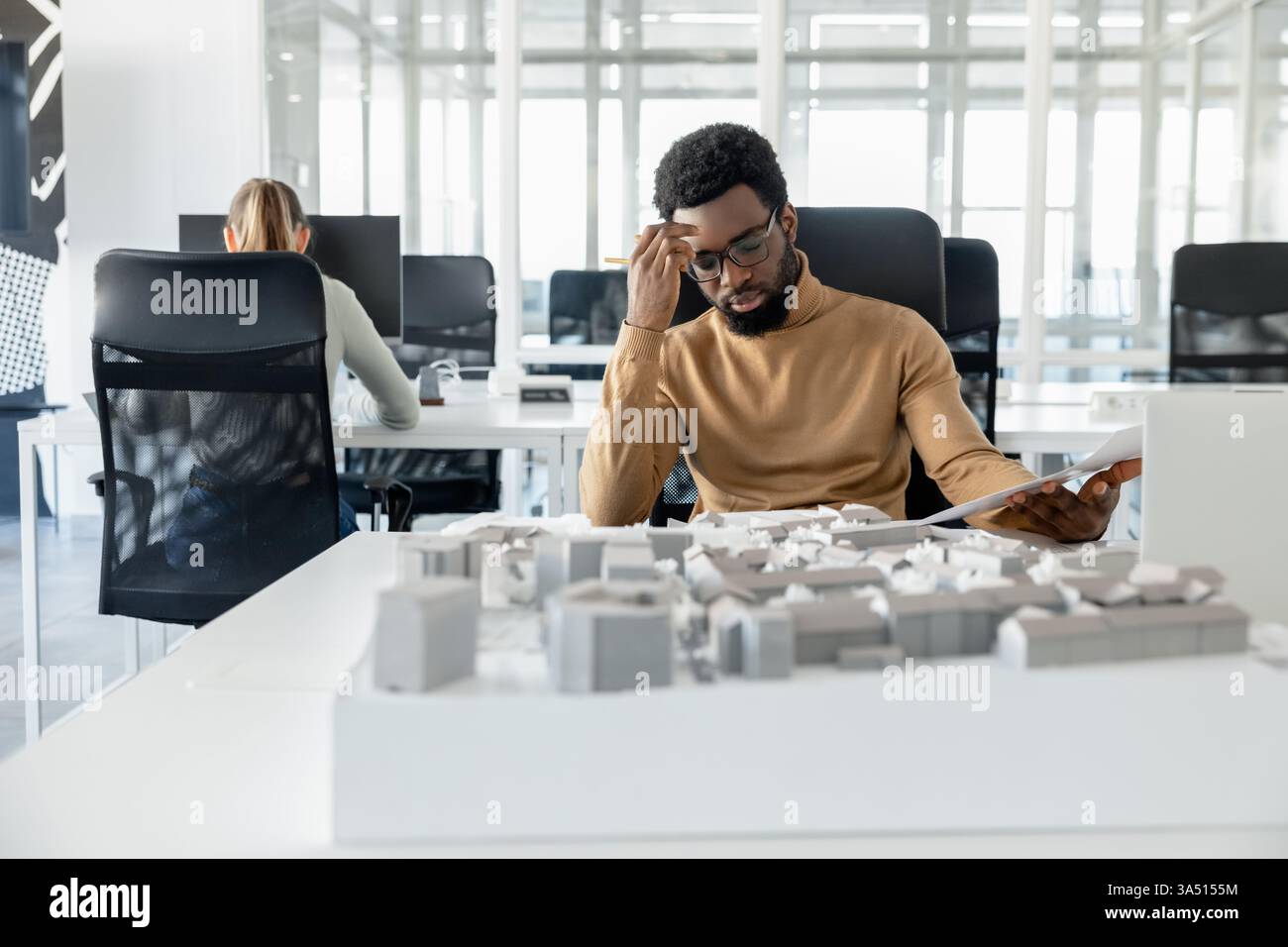 Dark-skinned young architect working in the office appears tired ...