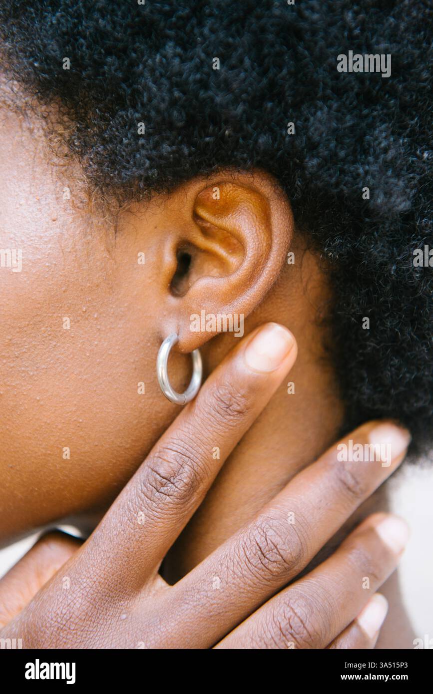 Black woman standing sideways touching neck against white wall on city ...