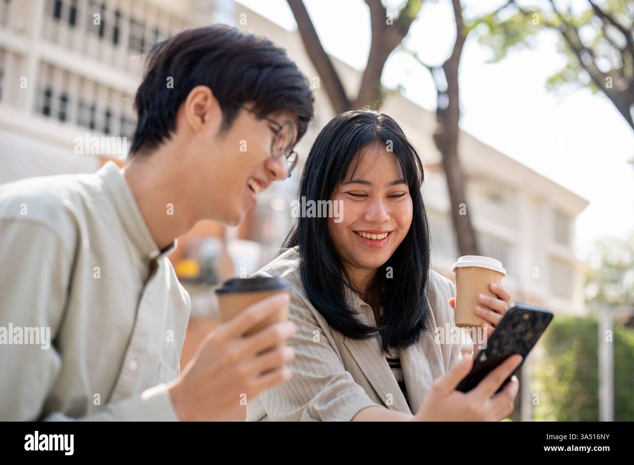 Two cheerful Asian friends are enjoying talking, watching videos, or ...