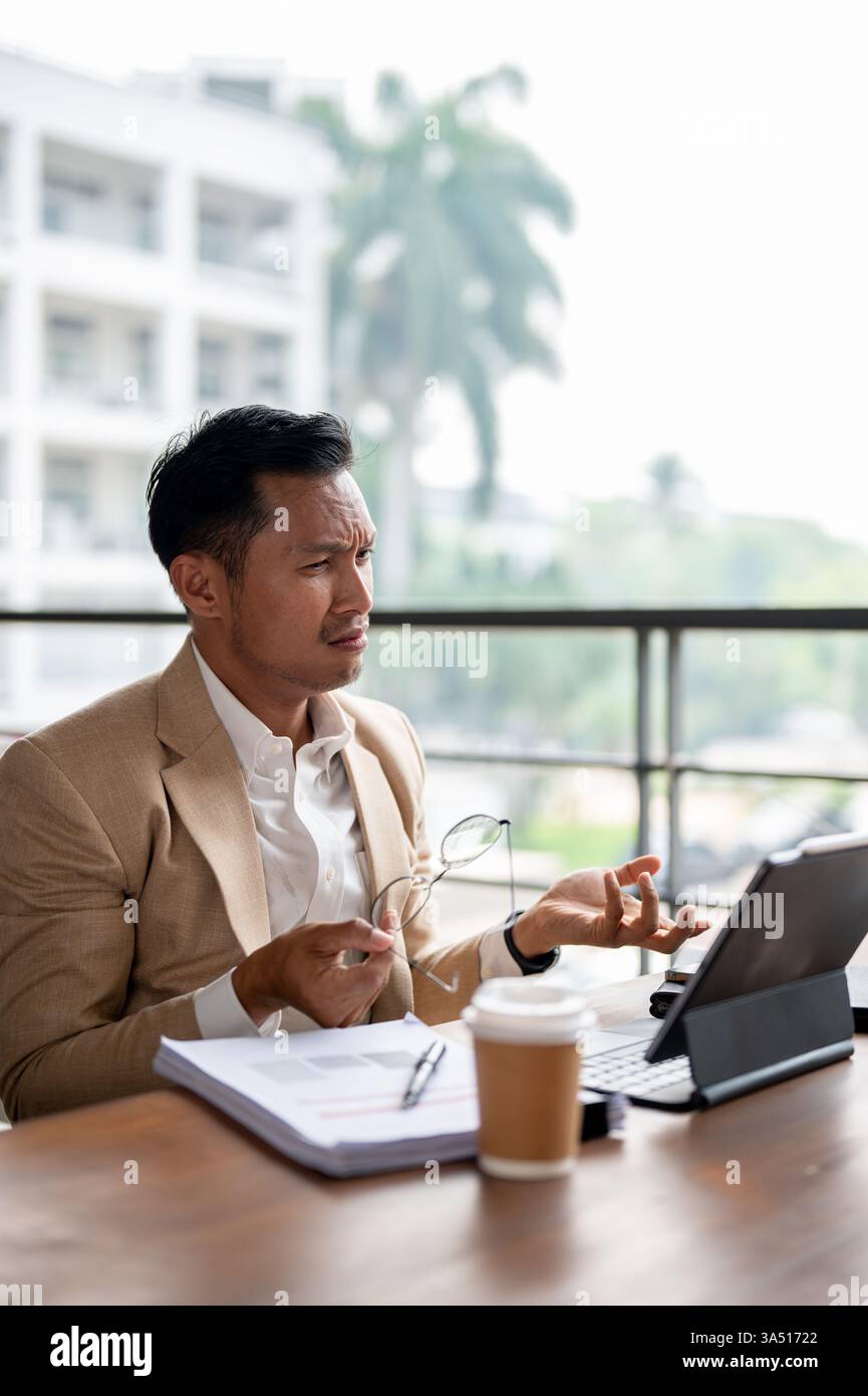 A confused, serious-looking Asian millennial businessman is staring at ...