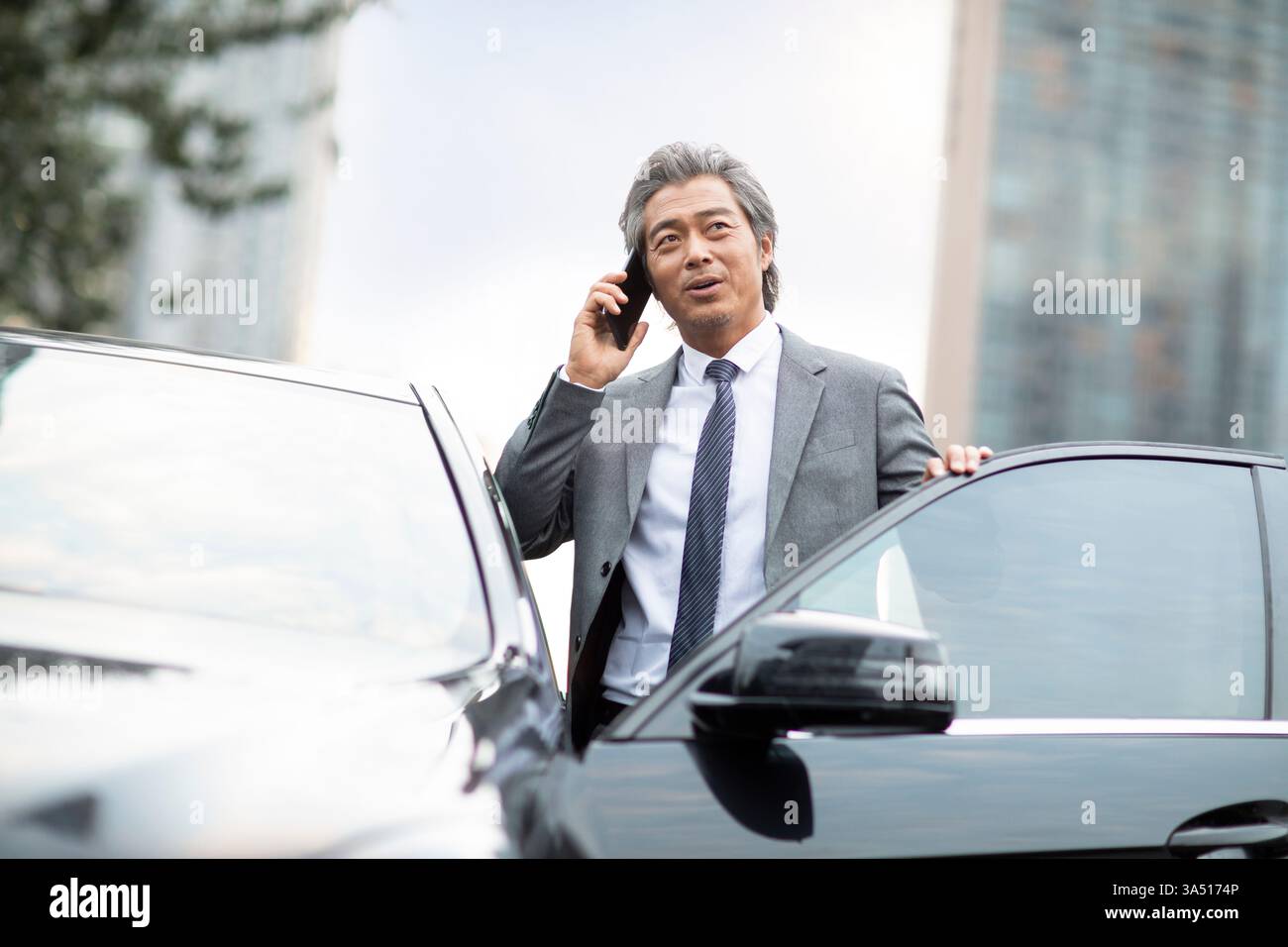Smiling Chinese businessman having phone call and looking away while ...