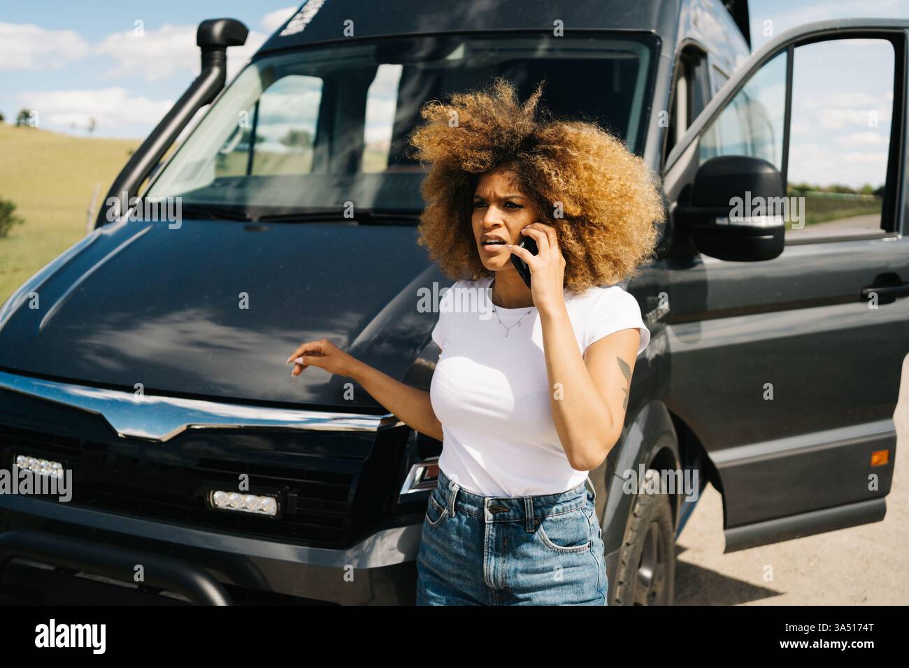 Worried Hispanic woman having phone call standing near parked camper ...