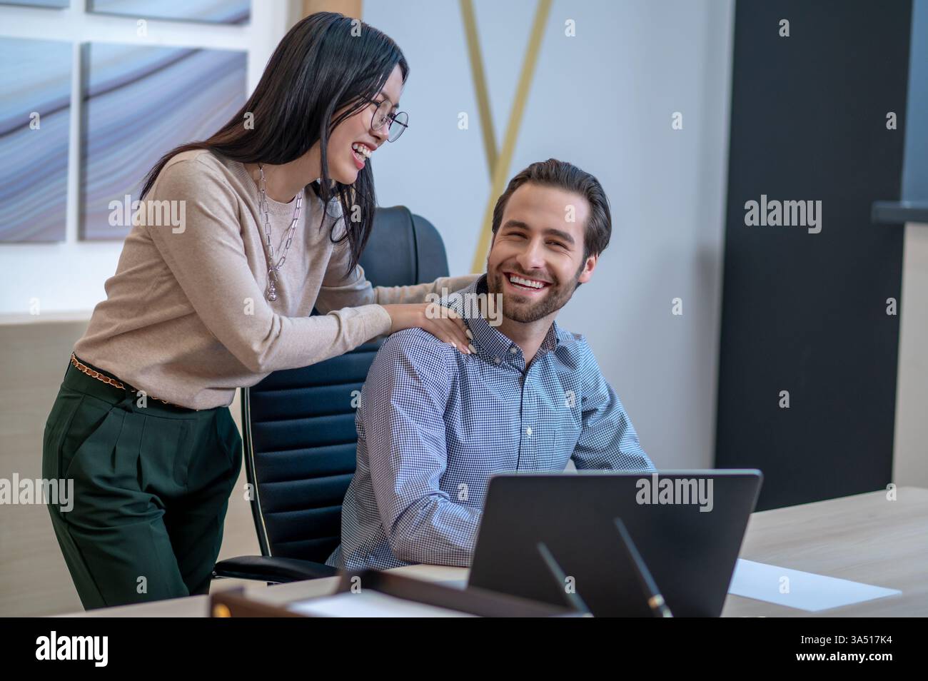 Joyful young female secretary standing beside her handsome pleased male ...