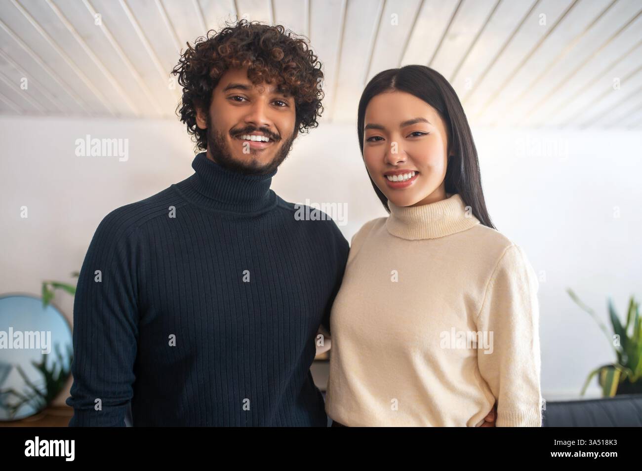 Smiling Asian man and Hispanic woman standing together at home during ...
