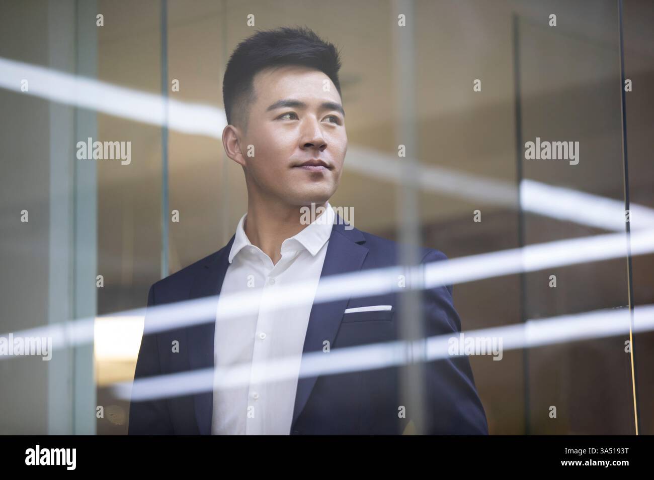 Chinese businessman looking away standing behind glass wall in office ...