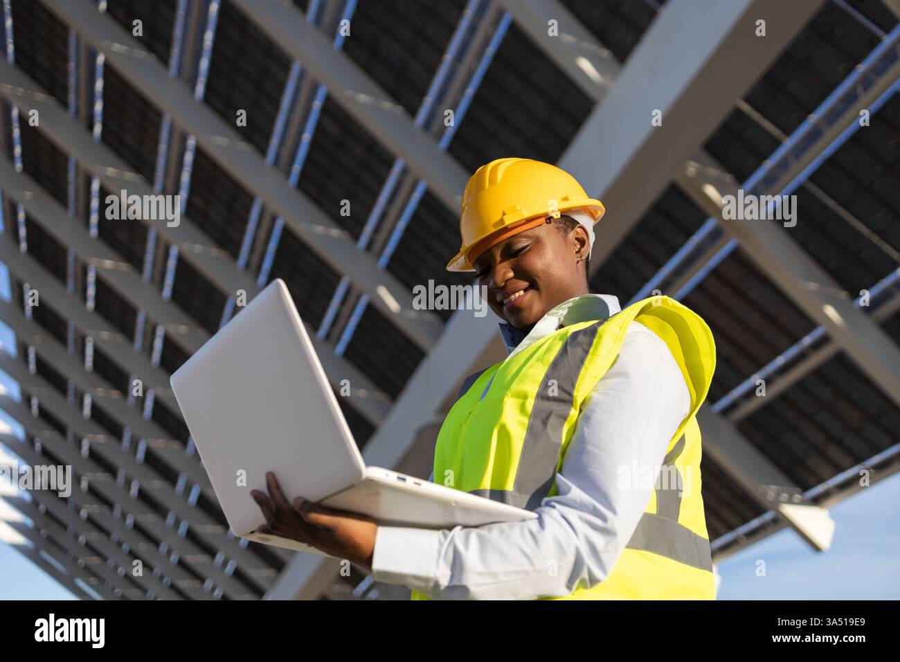 Black female engineer wearing a hard hat and safety vest standing at a ...