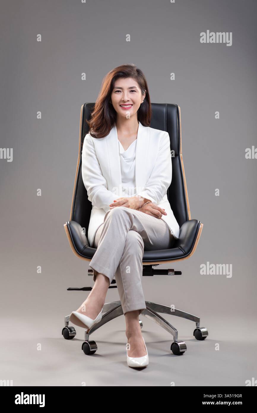 Smiling middle-aged Chinese business woman sitting with crossed legs on ...