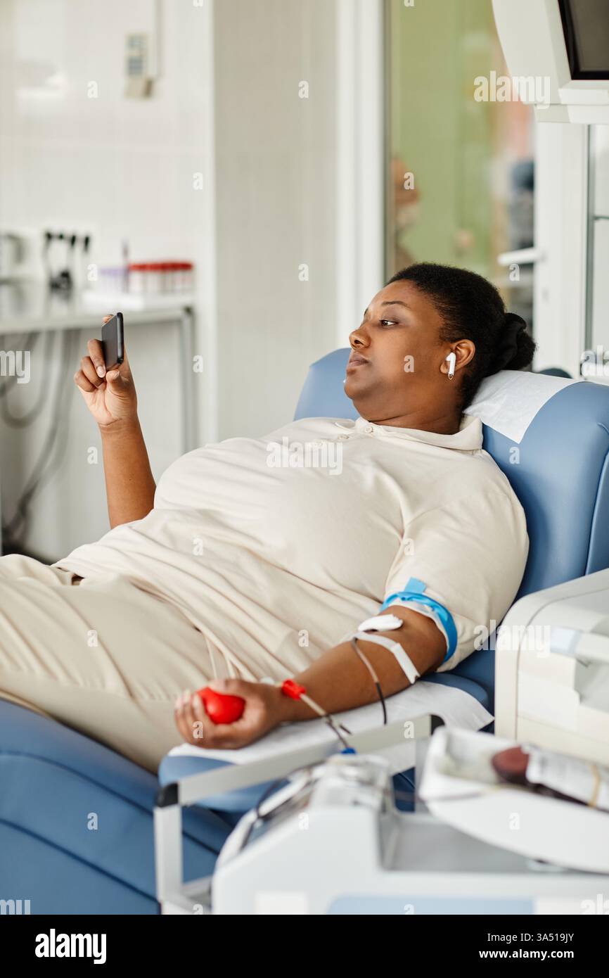 Vertical portrait of black young woman giving blood while laying in ...