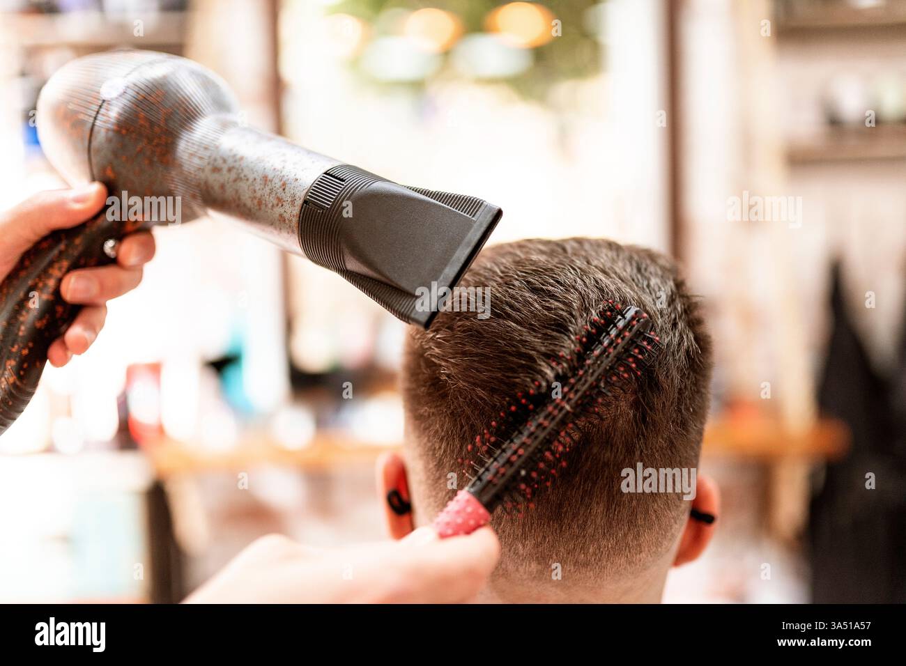 Hispanic male barber blow drying the hair of Hispanic male in ...