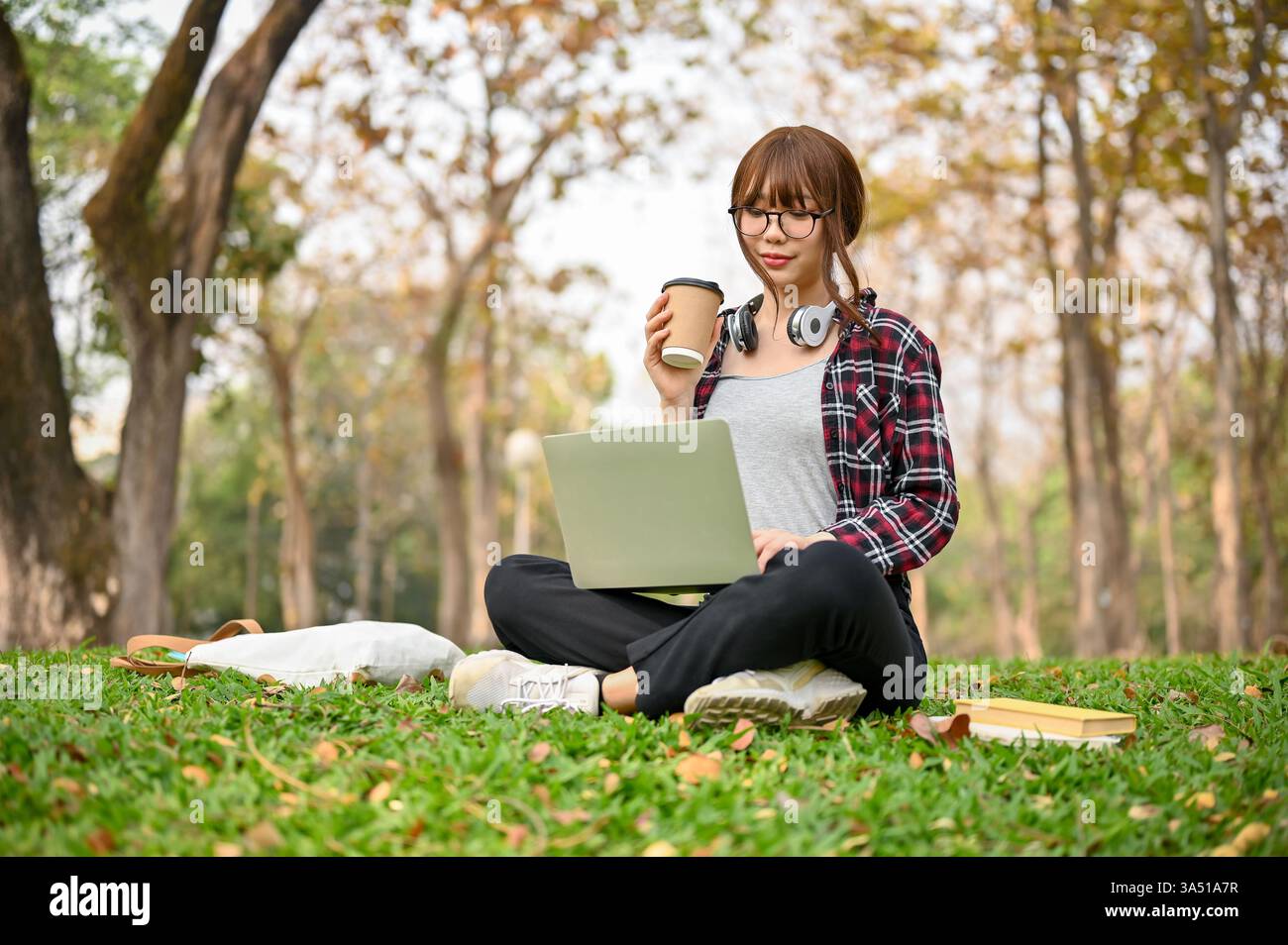 Smiling Asian female college student wearing eyeglasses and headphones ...