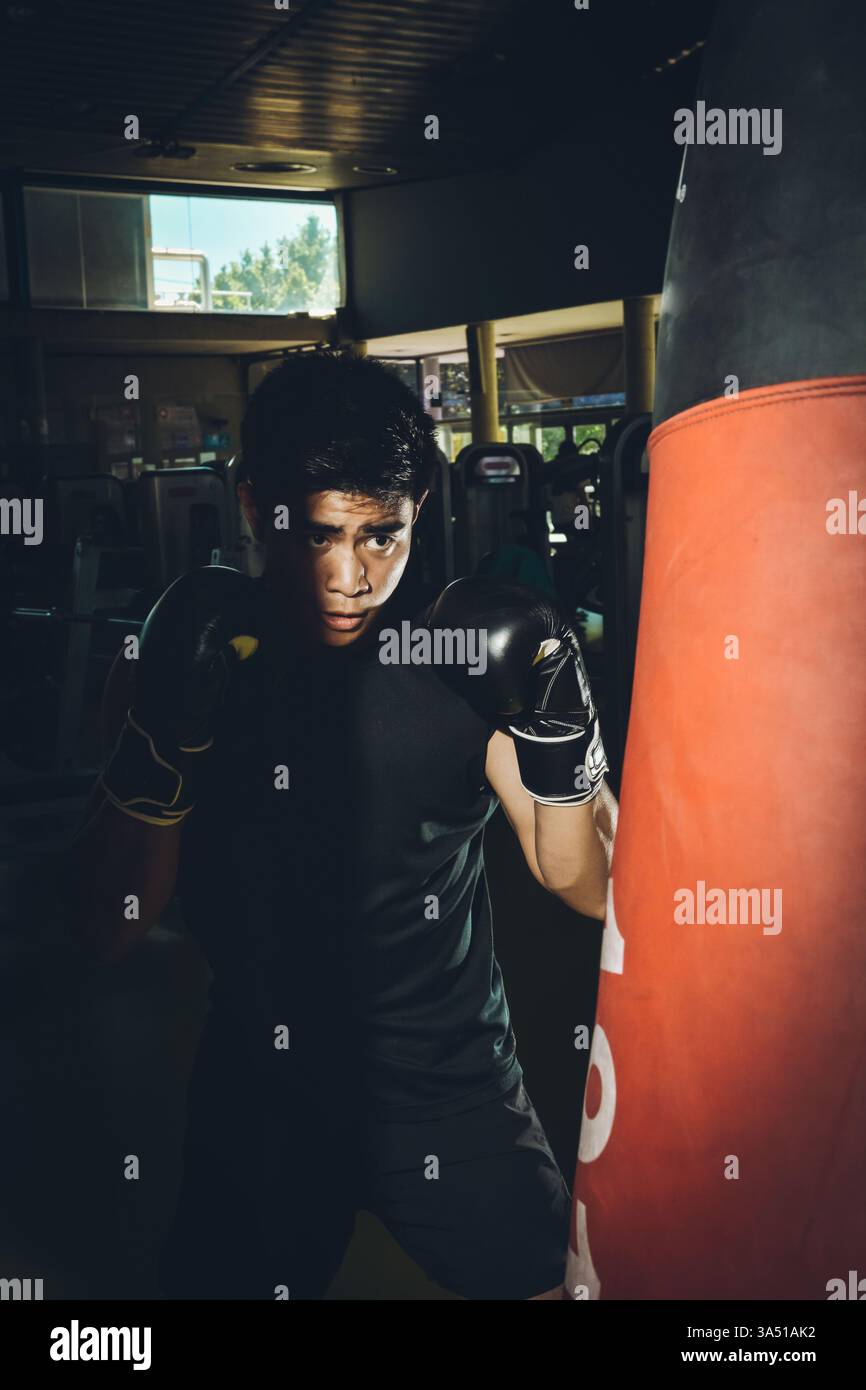 Asian male training boxing performing punches with punching bag in gym ...