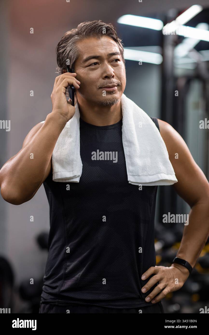 Smiling Middle aged Chinese man with towel on neck having phone call ...