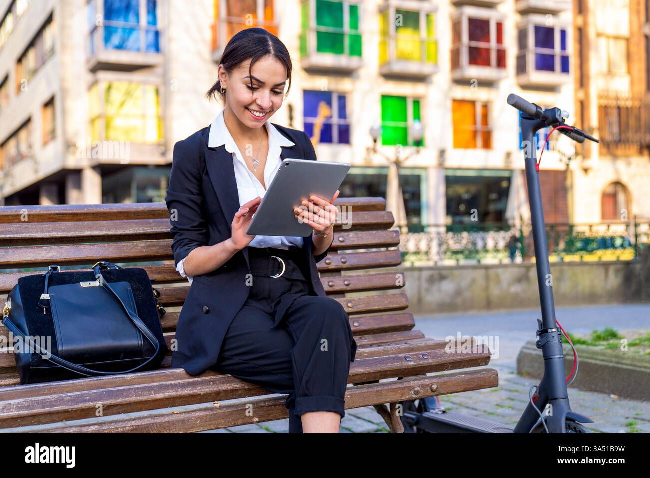 Smiling Asian female using tablet sitting with crossed legs on outdoor ...