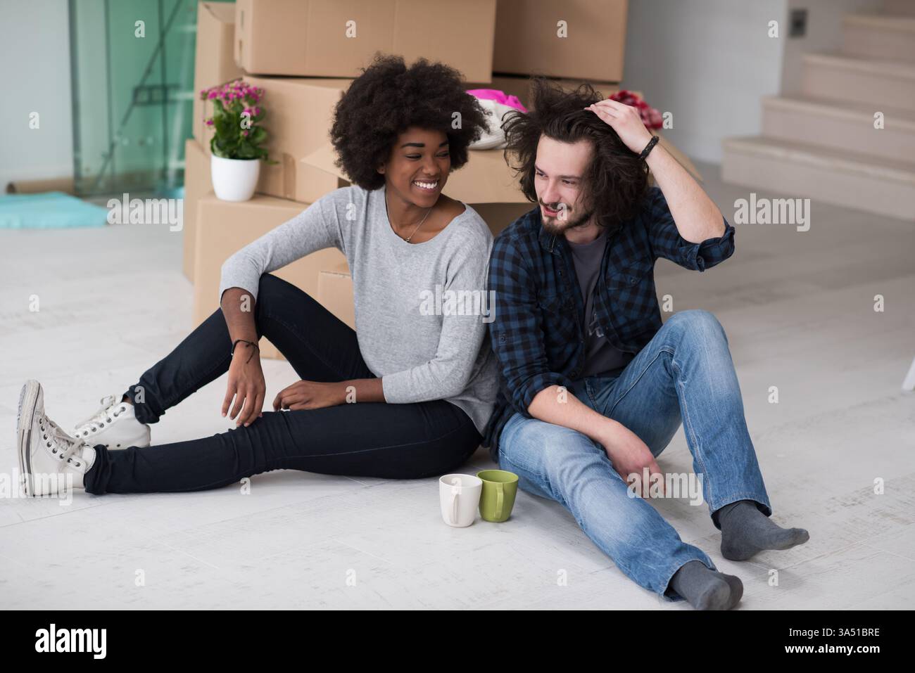 Relaxing in new house. Cheerful young multiethnic couple sitting on the ...