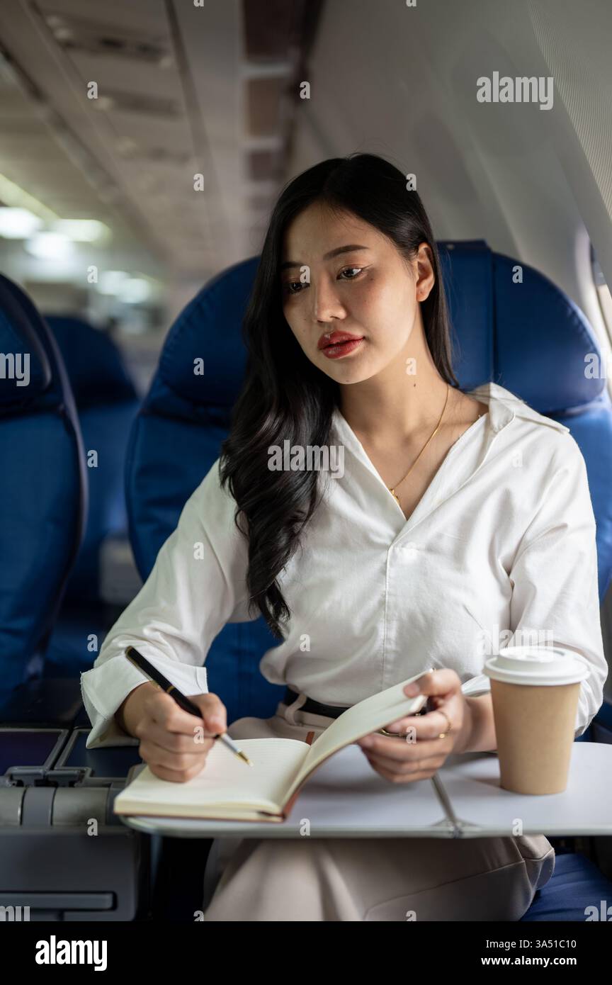 Serious Asian business woman holding pen writing in notebook looking ...