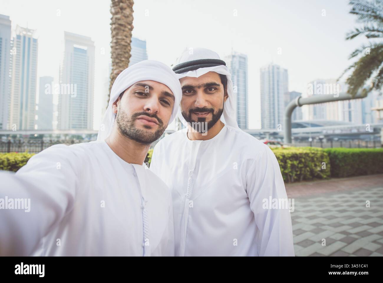 Two young Middle Eastern businessmen in kandura walk along Dubai Marina ...