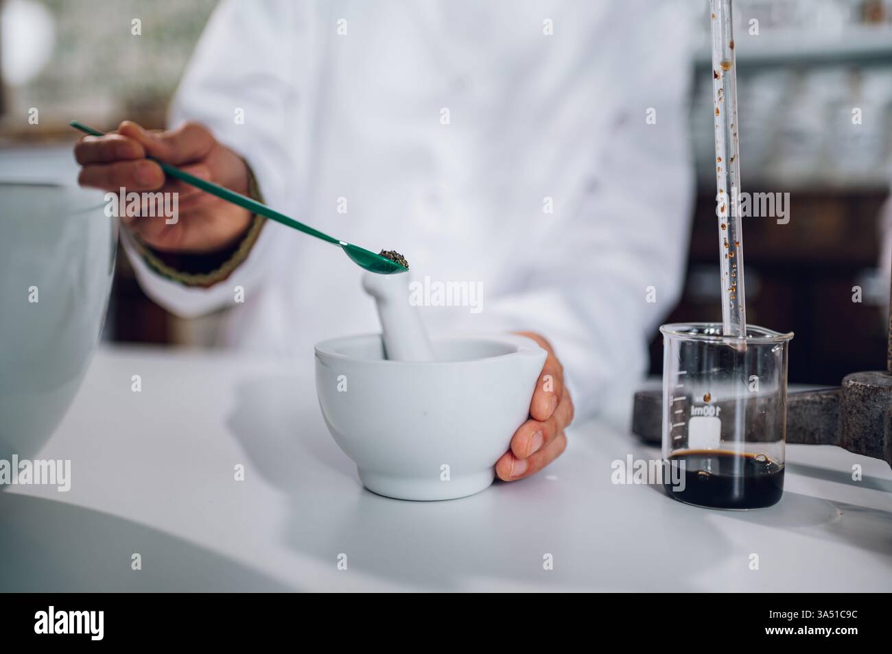 Close up of a chemist's hands adding a drug ingredient to a mortar in a ...