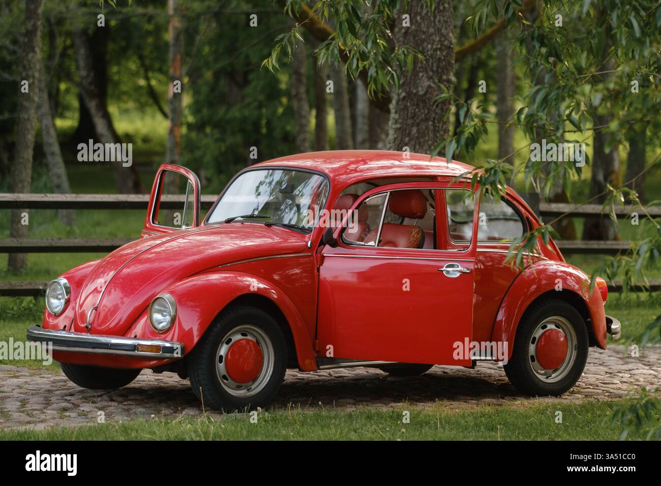 A bright red vintage car is parked on a stone pathway surrounded by ...