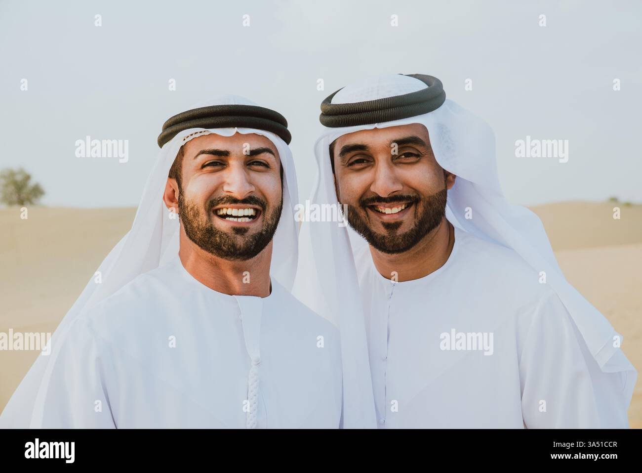 Smiling Arab men wearing kandura standing together on desert during ...