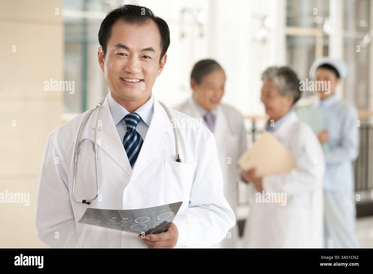 Chinese doctor holding CAT scan with doctors and nurse in background ...