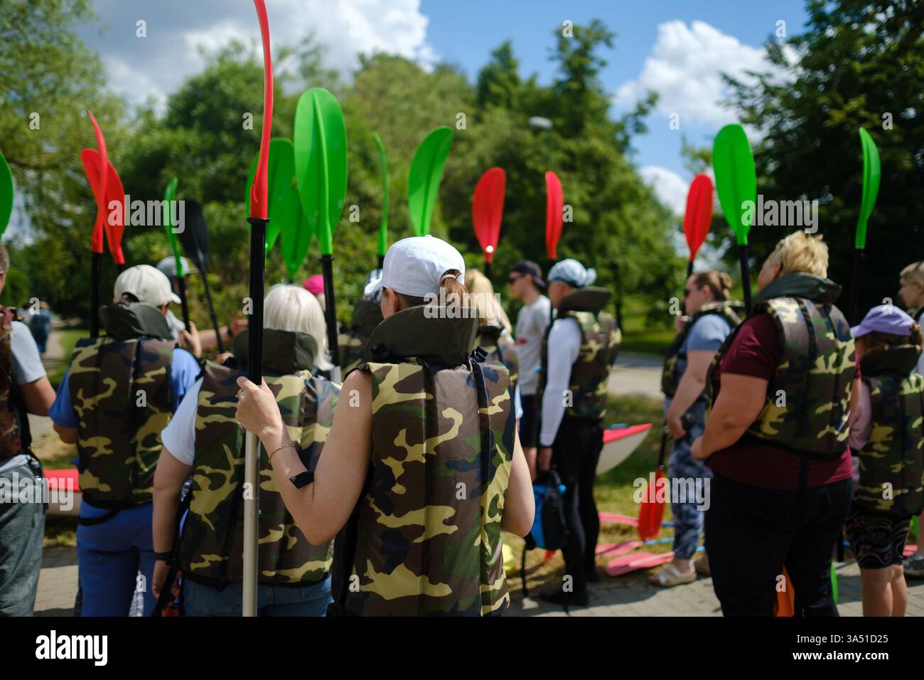 Groups of people in life vests and colorful paddles gather in a sunny ...