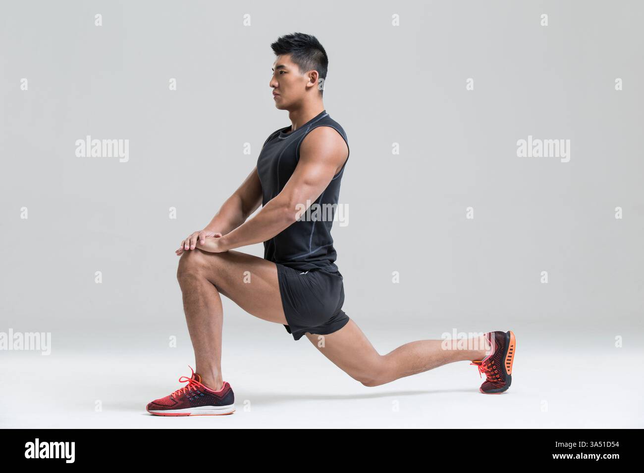 Chinese man doing stretching exercise against gray background in studio ...