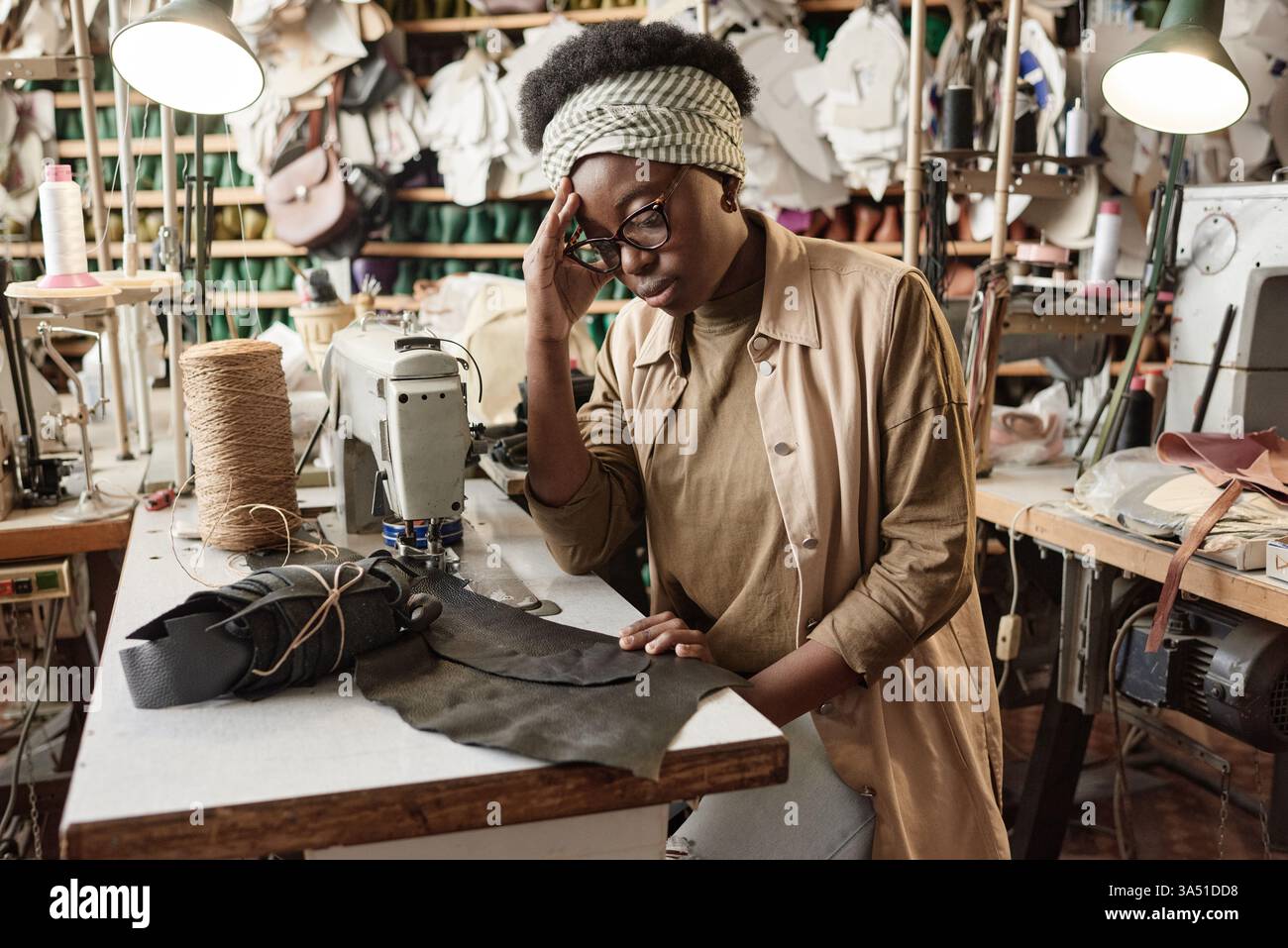 African tailor sitting at the table with fabric and sewing machine and ...