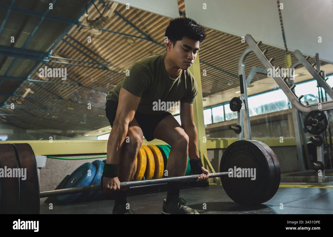 Asian male doing deadlift with heavy barbell during workout in empty ...