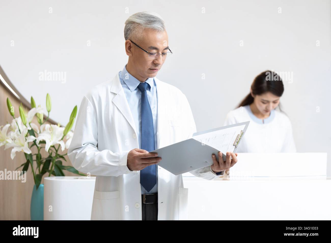 Chinese male doctor reading clipboard while standing with Chinese ...