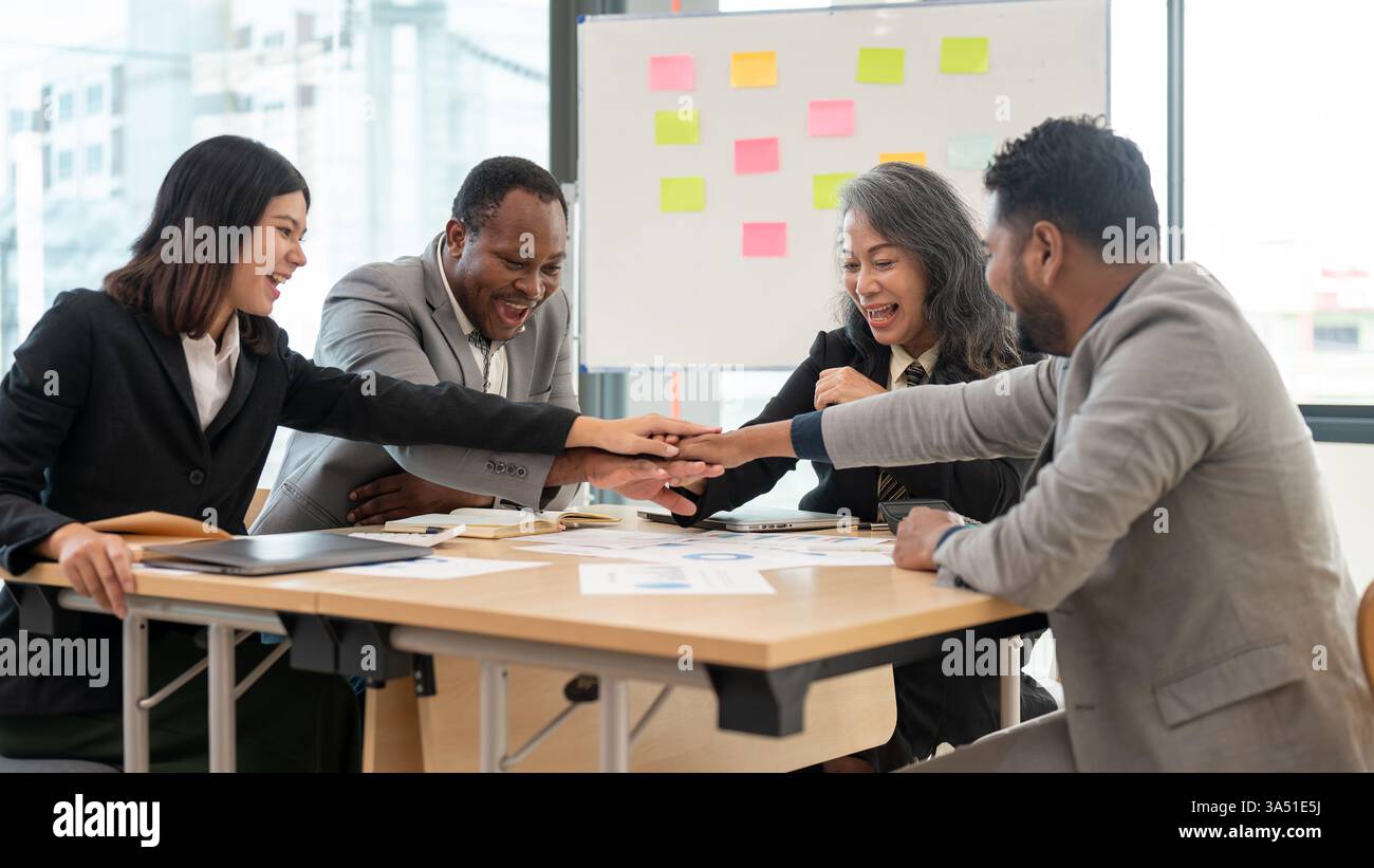 Multiracial team in a meeting, joining hands in a show of unity after a ...