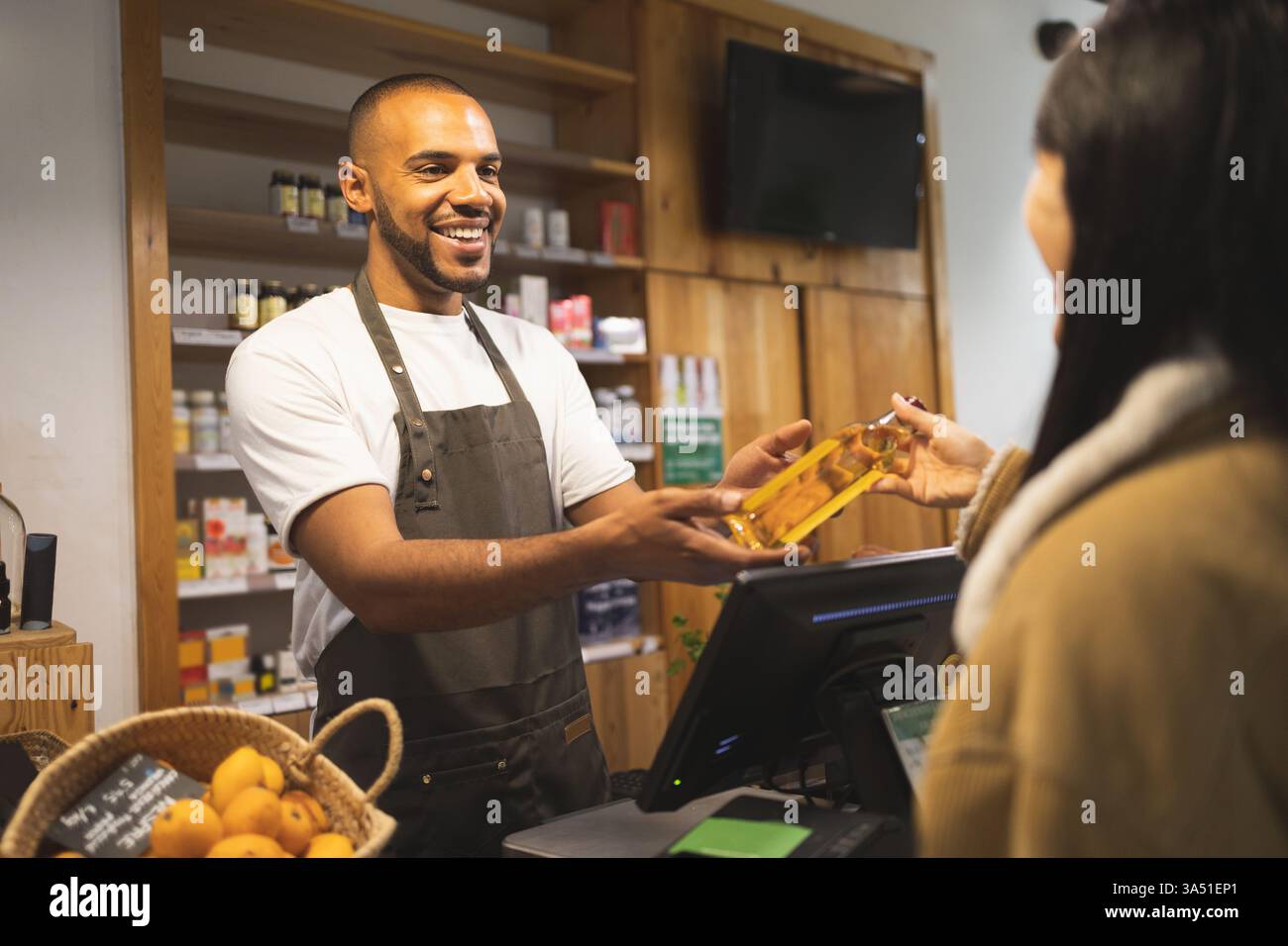 Smiling Black salesman wearing apron giving bottle of oil to Asian ...
