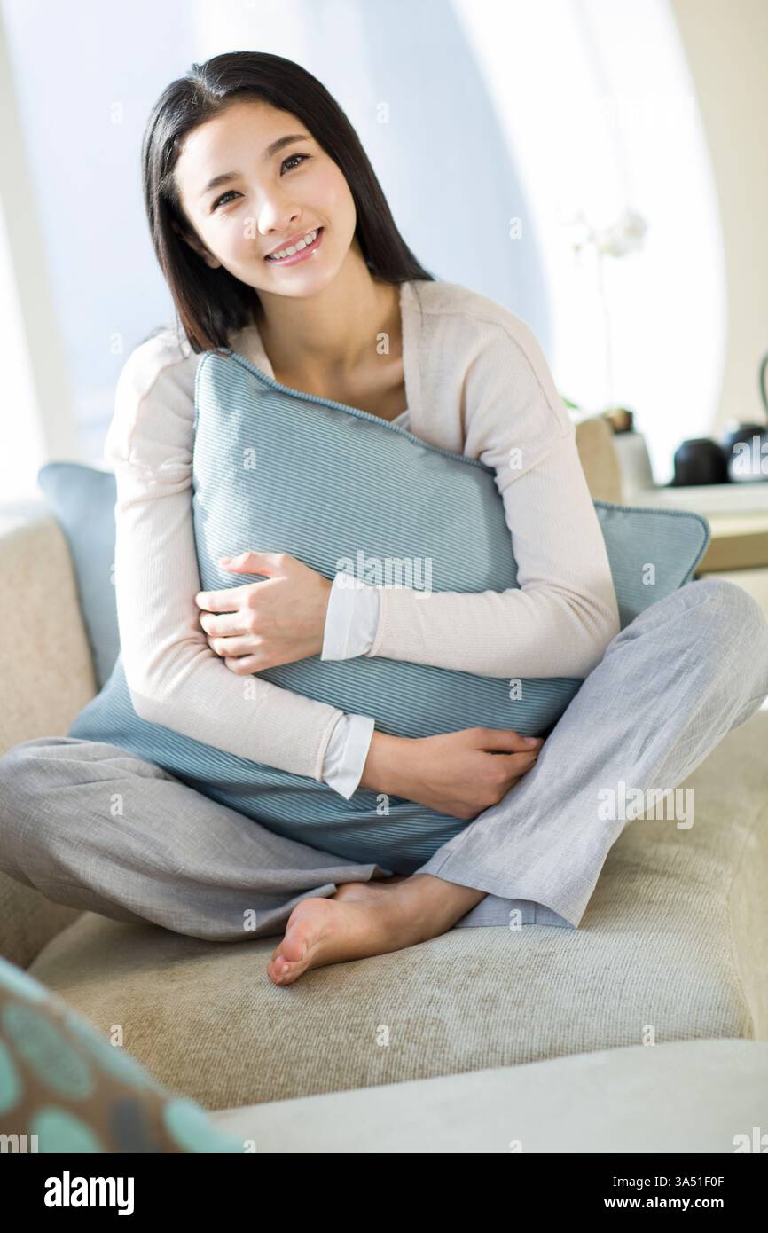 Happy young Chinese woman sitting on sofa Stock Photo - Alamy