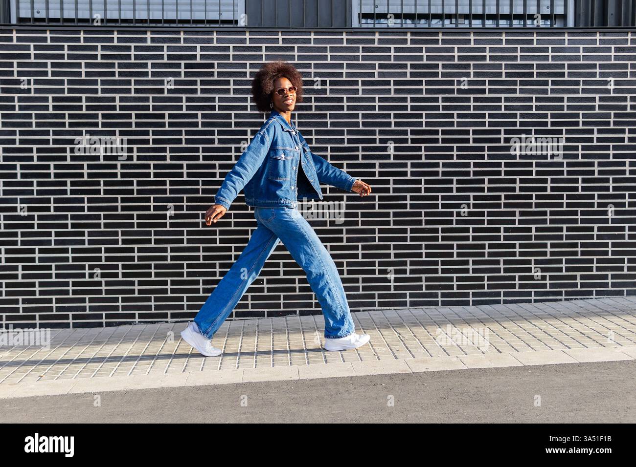 A confident African American woman in full denim strides forward, her ...