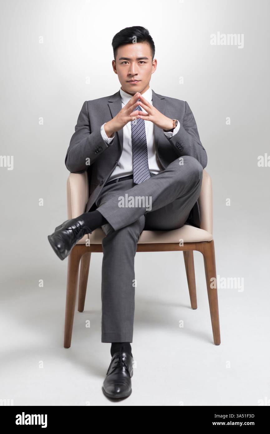 Chinese businessman sitting with crossed legs and finger tips together ...