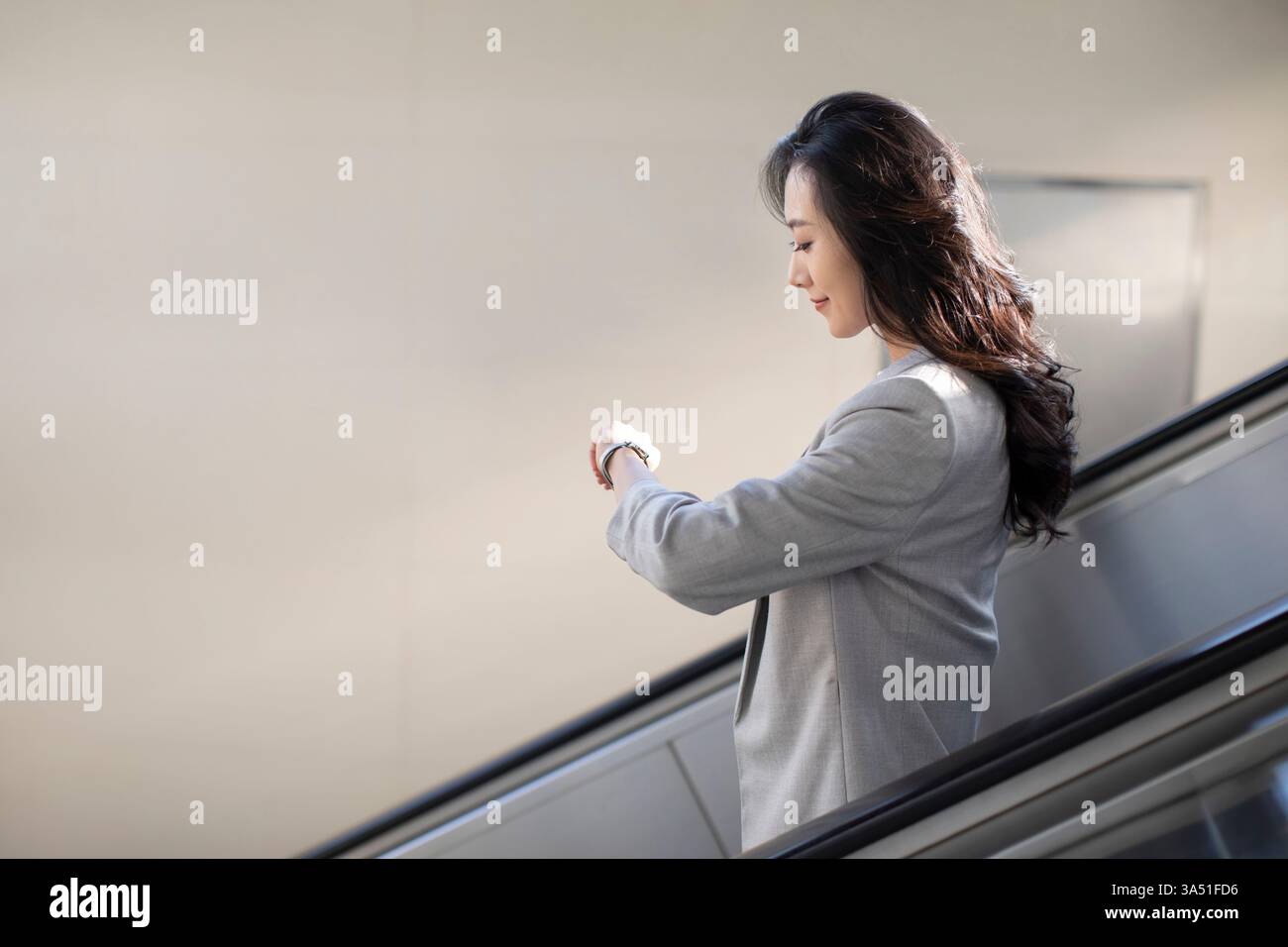 Chinese business woman looking at her watch standing on escalator in ...