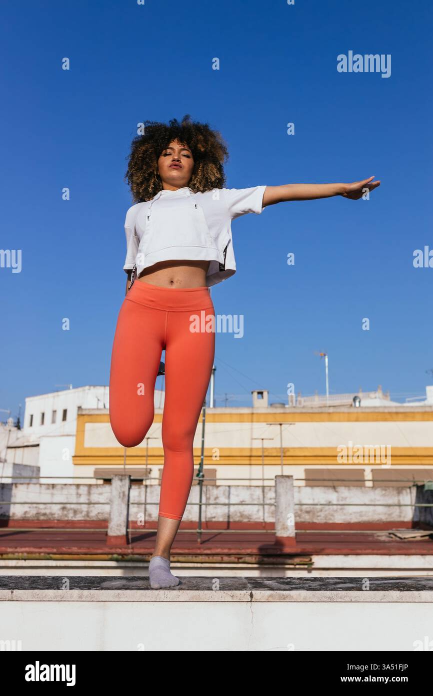 Black woman standing on one leg closed eyes practicing yoga on rooftop ...
