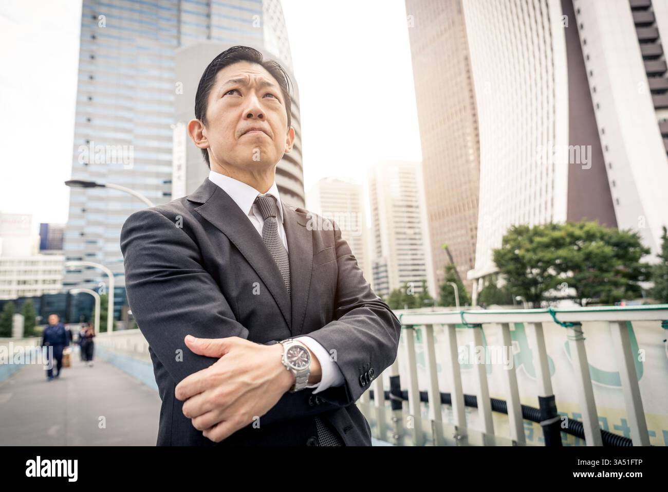 Serious Asian businessman standing on a city bridge during daytime with ...