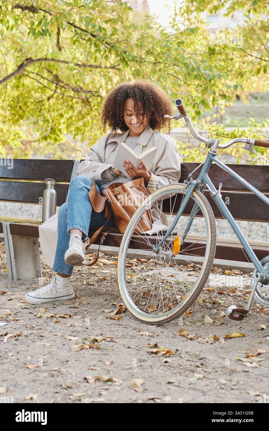 Full body of young smiling female student with curly hair sitting on ...