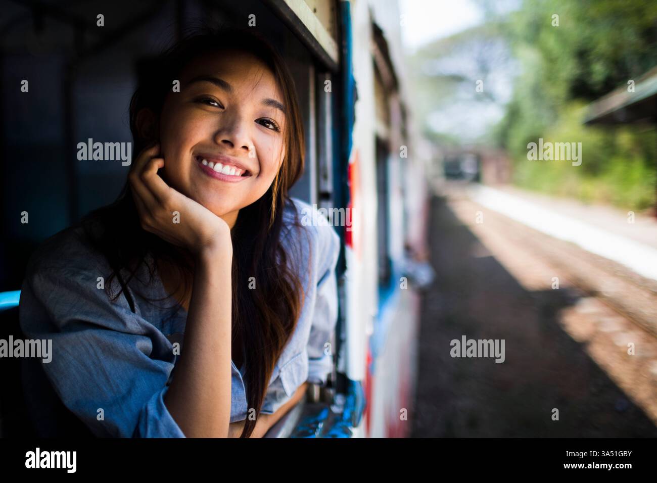 Asian woman sitting leaning chin on hand looking out of train window ...
