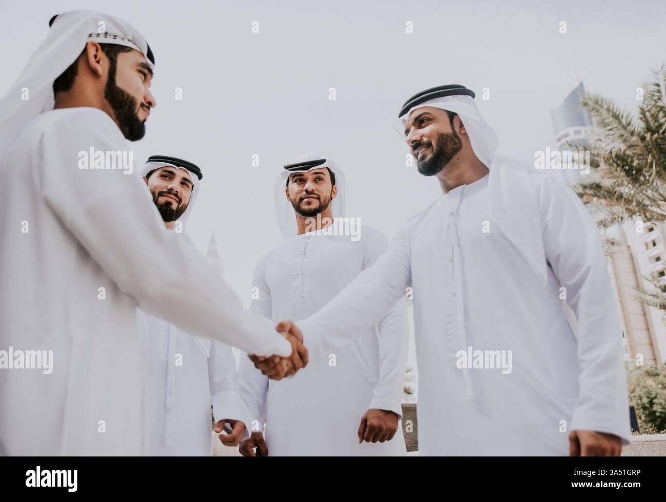 Smiling Middle Eastern men doing handshake near male friends standing ...