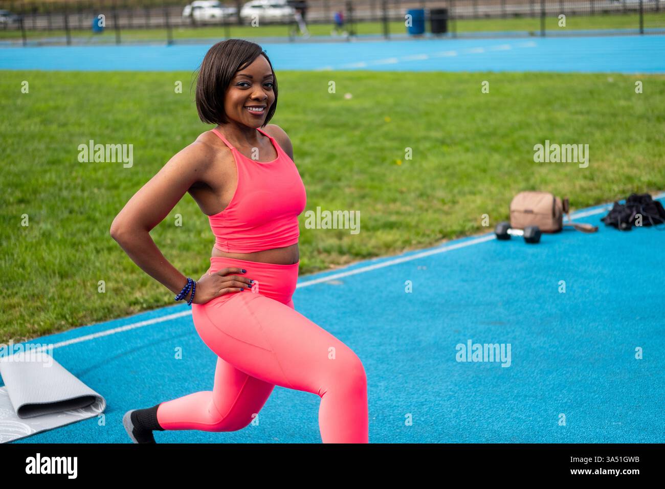Smiling Black woman in pink activewear bending her legs with hands on ...
