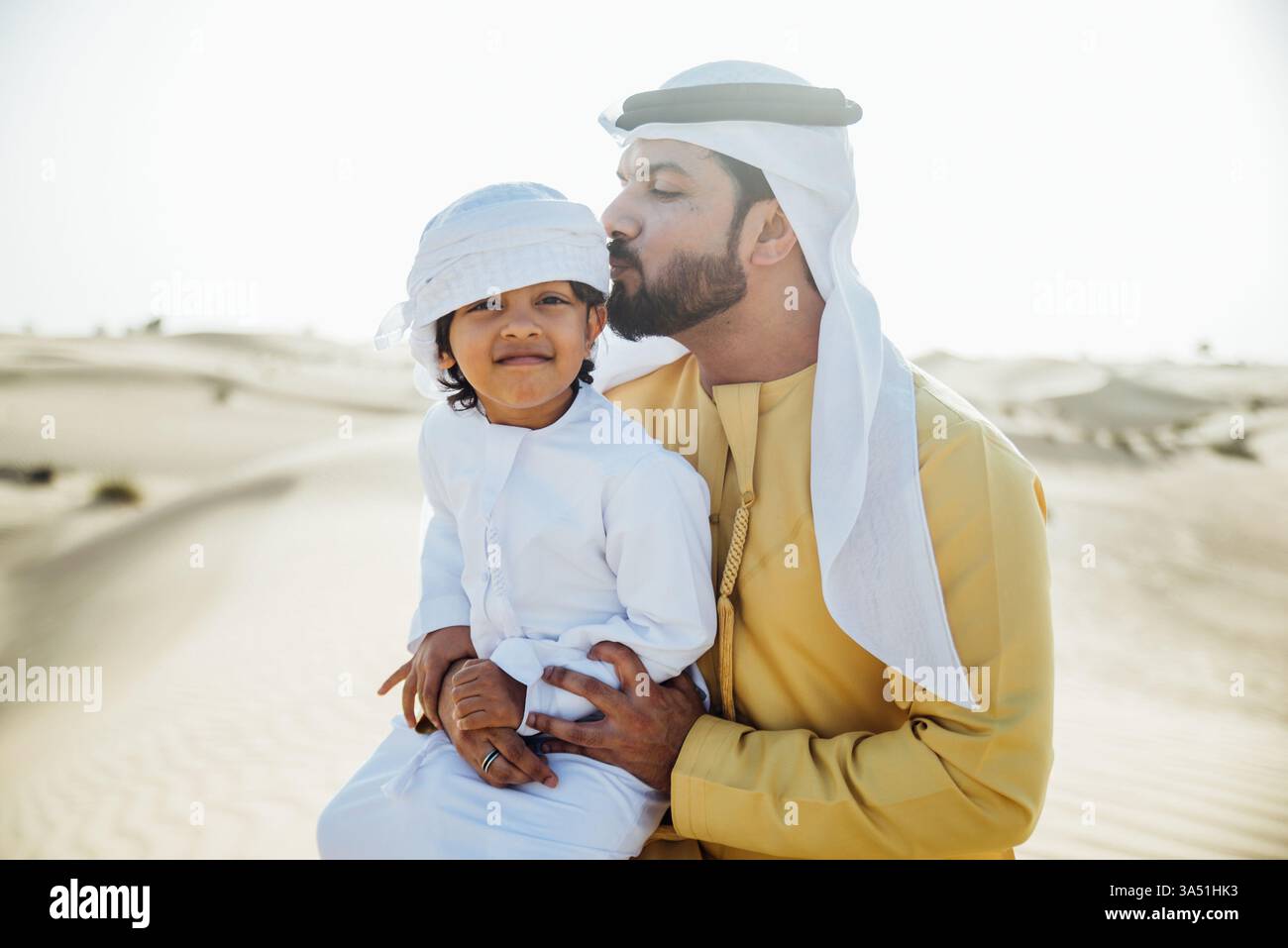Middle Eastern father carrying son on lap kissing his forehead while ...