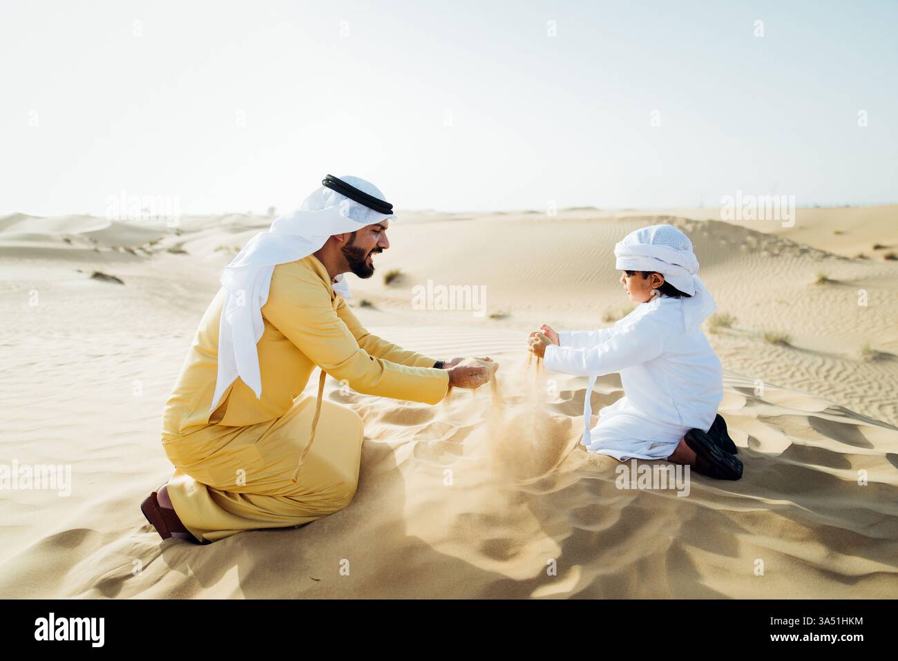 Cheerful Middle Eastern father kneeling and playing sand with son on ...