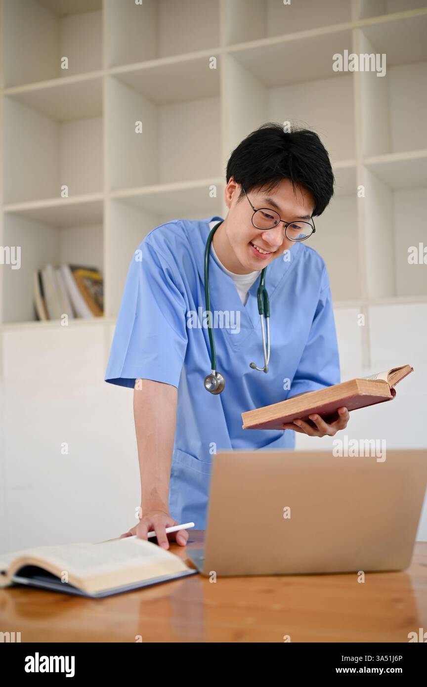 Smart young Asian male medical student leaning on table, using laptop ...